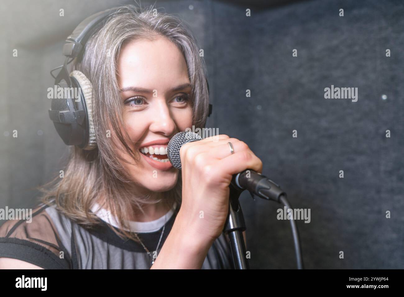 Woman singing into microphone in recording studio, wearing headphones ...