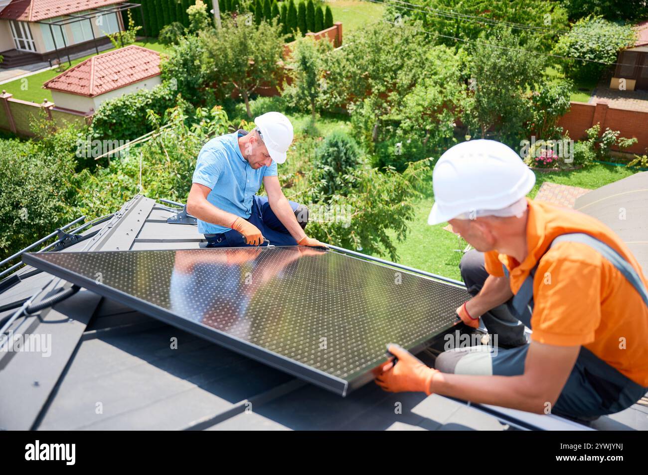 Workers building photovoltaic solar panel system on rooftop of house. Men technicians in helmets ...