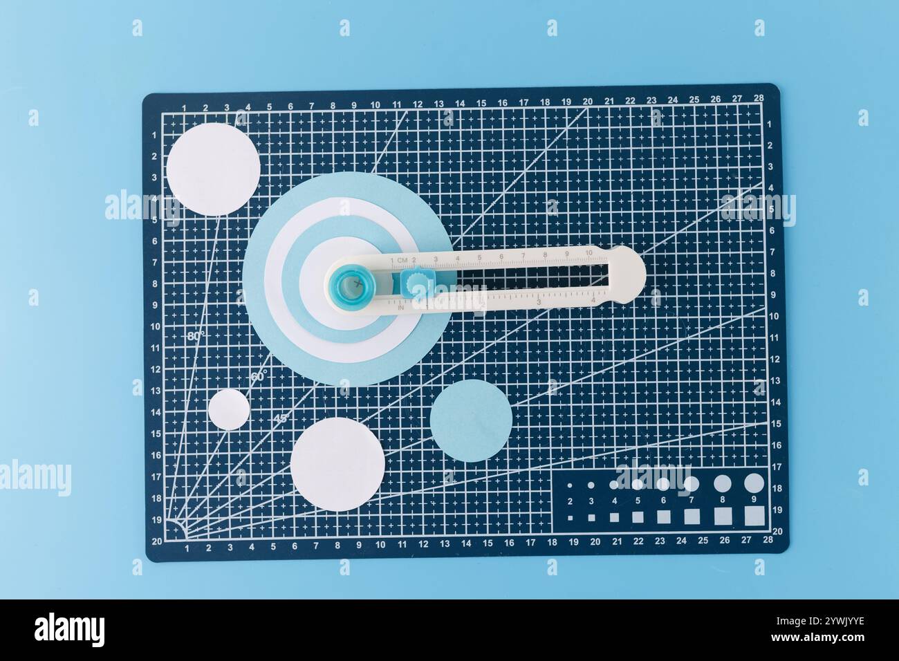 Paper circle cutter tool with blue cutouts on a mat with grid on blue ...