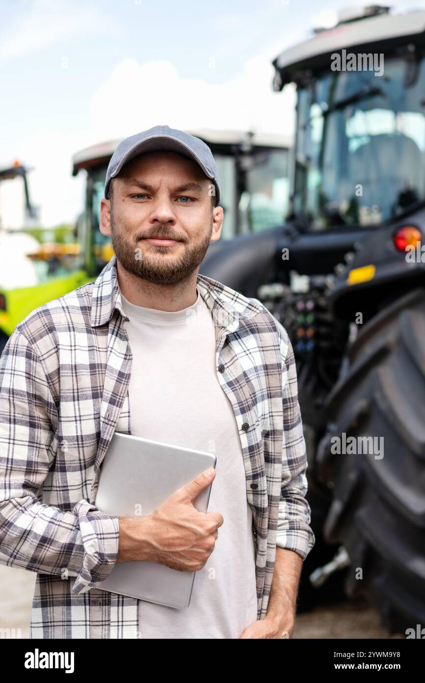 Vertical portrait man farm worker with digital tablet against tractor ...