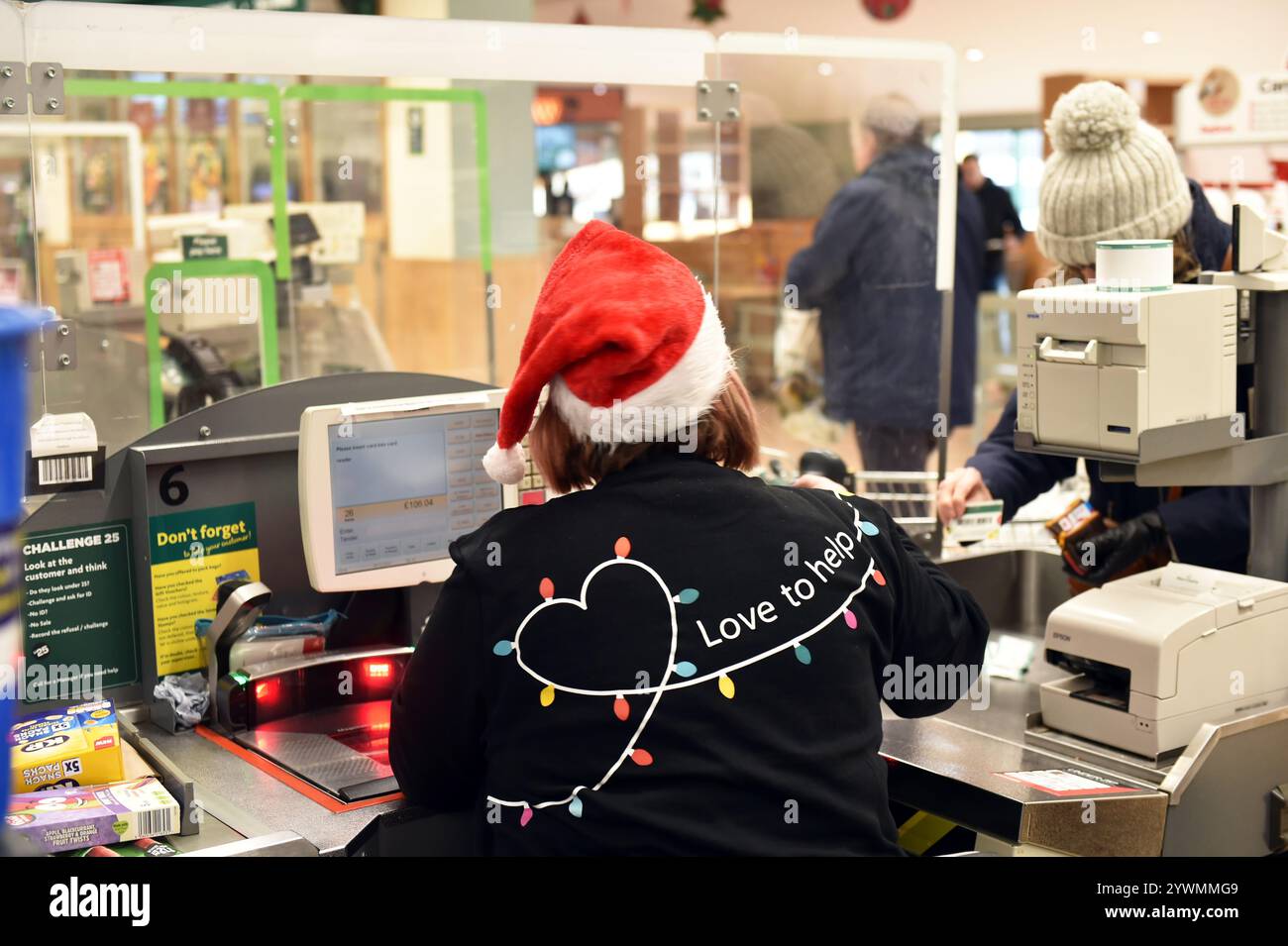 A supermarket shop assistant works on the tills at Christmas in a ...