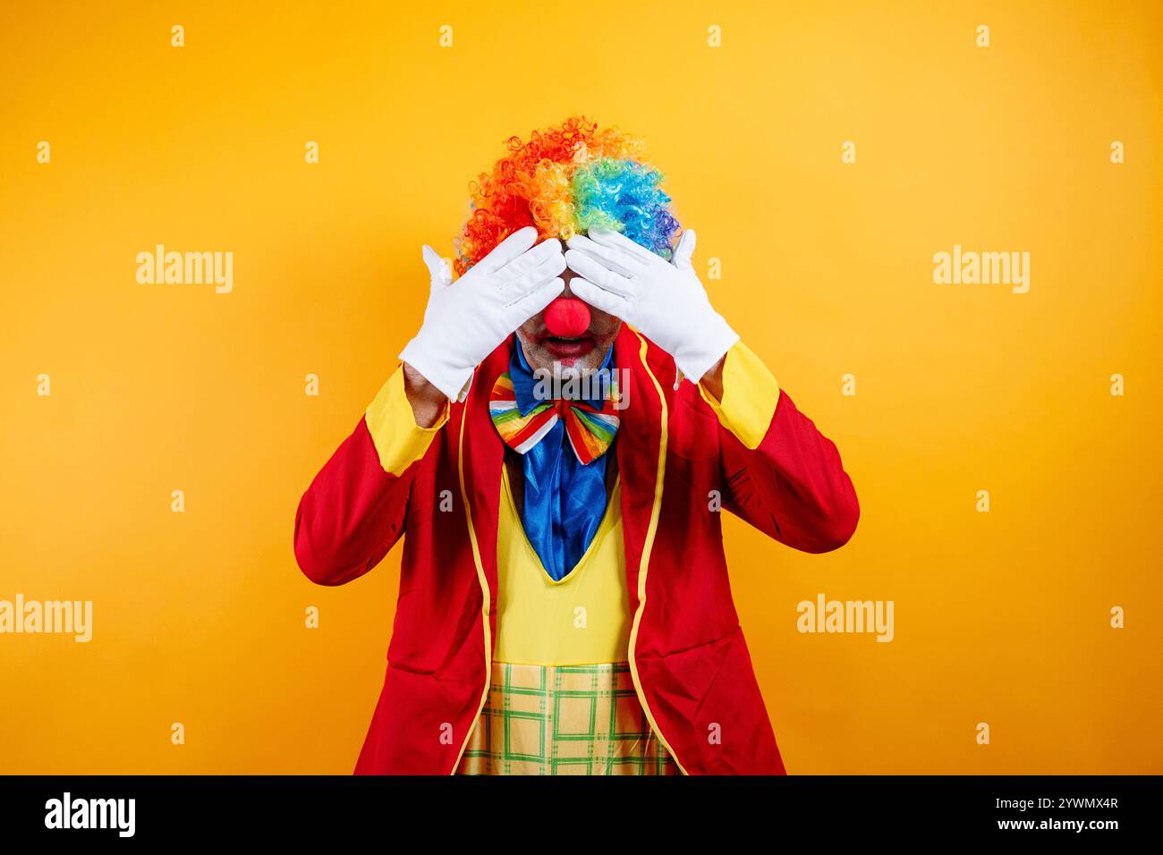 Playful clown hides face, bright yellow background Stock Photo - Alamy