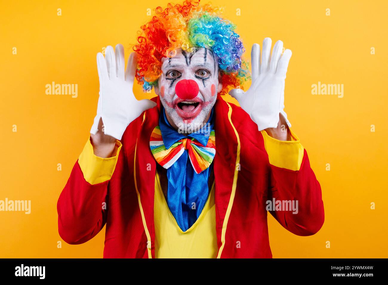 Shocked clown with rainbow wig, wide-eyed, hands up Stock Photo - Alamy