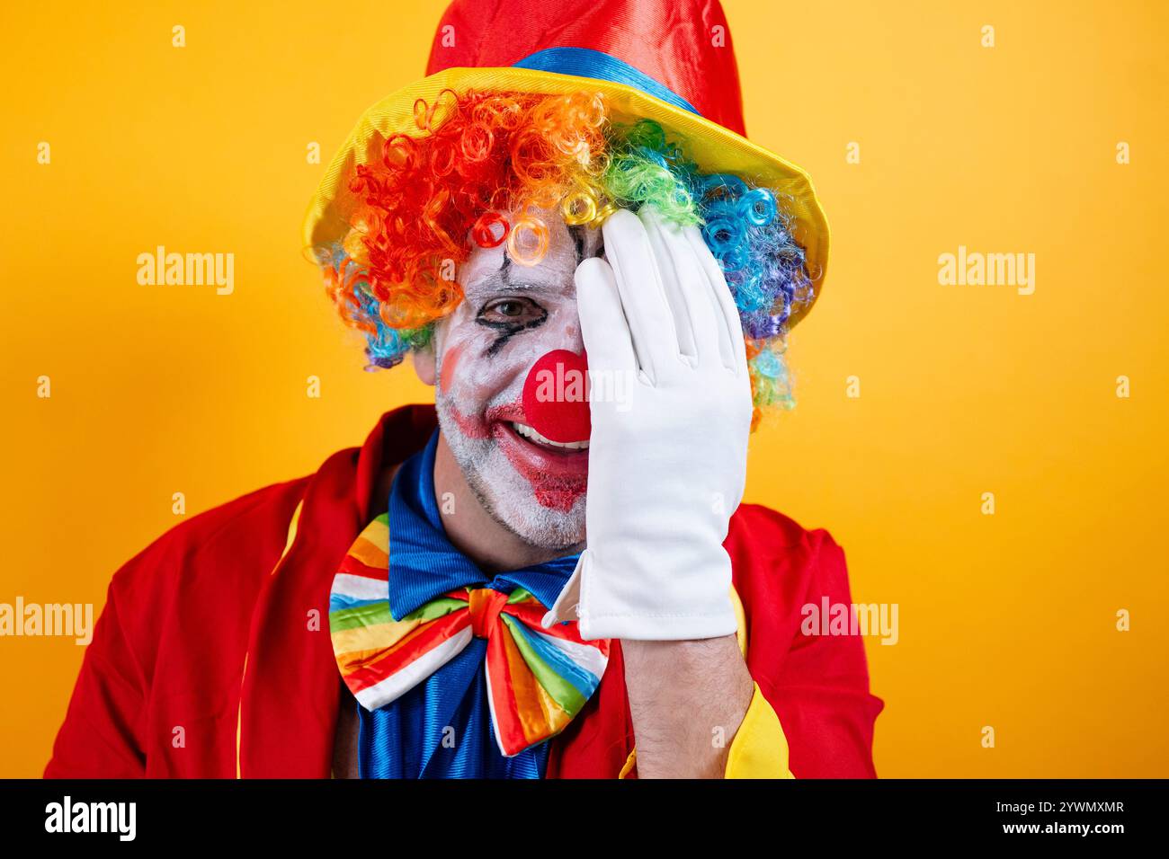 Playful clown hides face, bright yellow background Stock Photo - Alamy