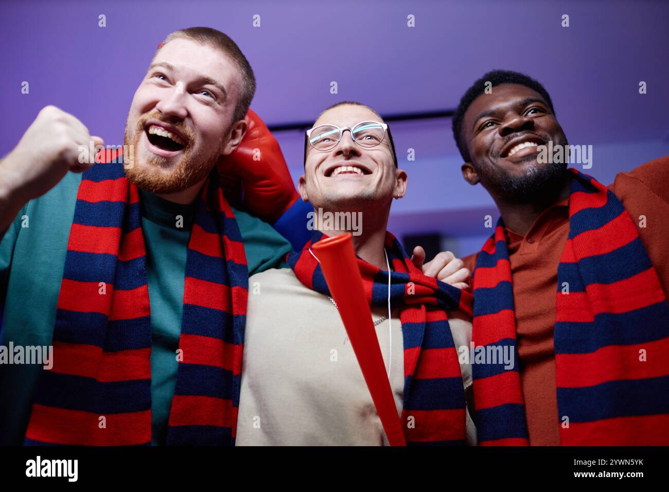 Low angle portrait of three excited sports fans huddling and cheering ...
