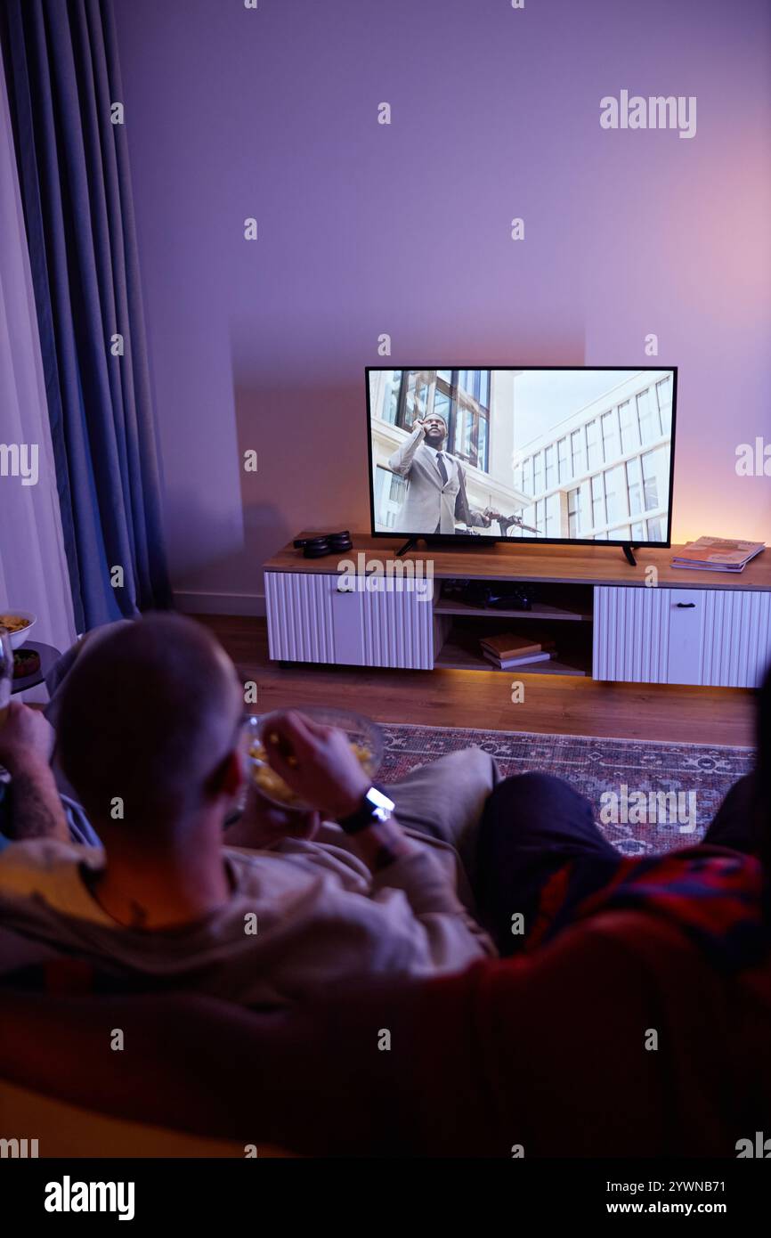 Vertical back view of friends watching Tv at night in dark room while ...