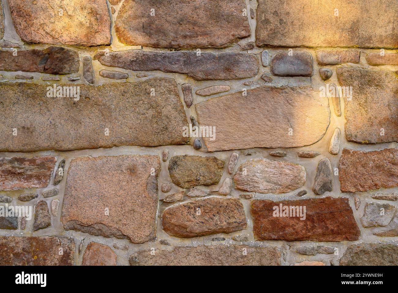 A rustic stone wall composed of various shapes and hues creates a warm ...