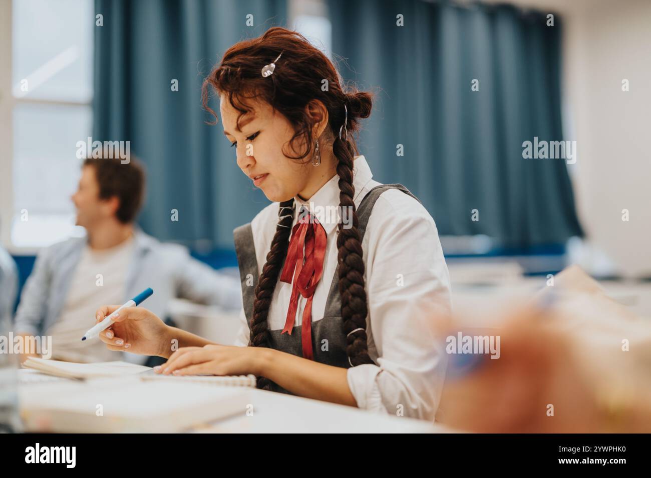 Focused student taking notes in a classroom setting during lecture ...