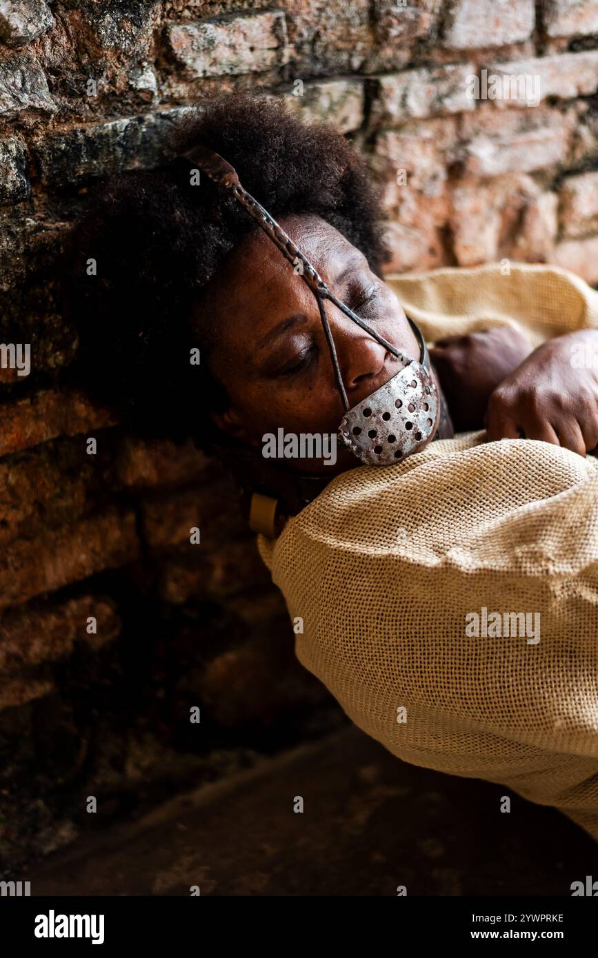 Black woman with an iron mask on her mouth and chained, leaning against ...