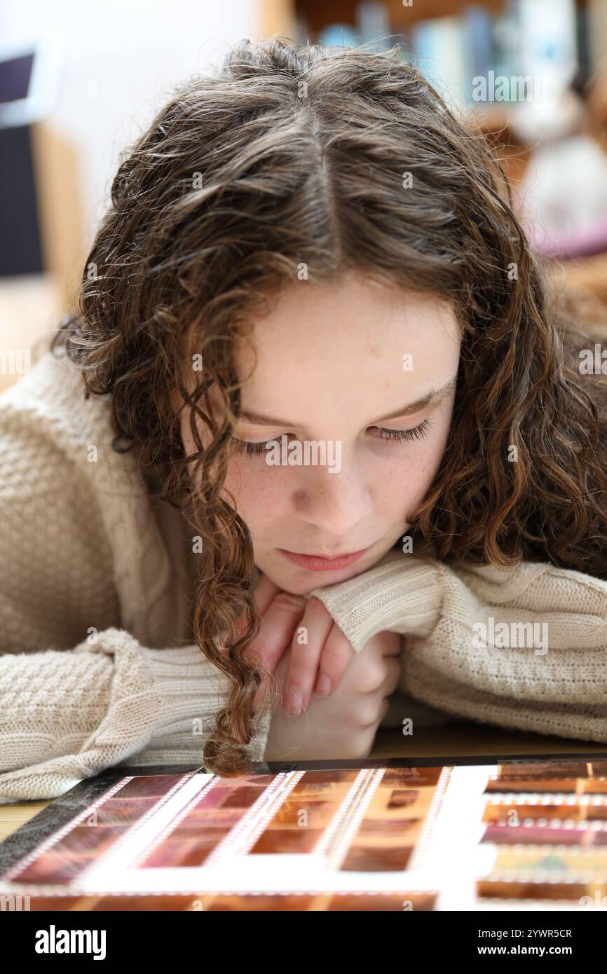 Teenage girl looking at 35mm film negatives on a lightbox lying on ...