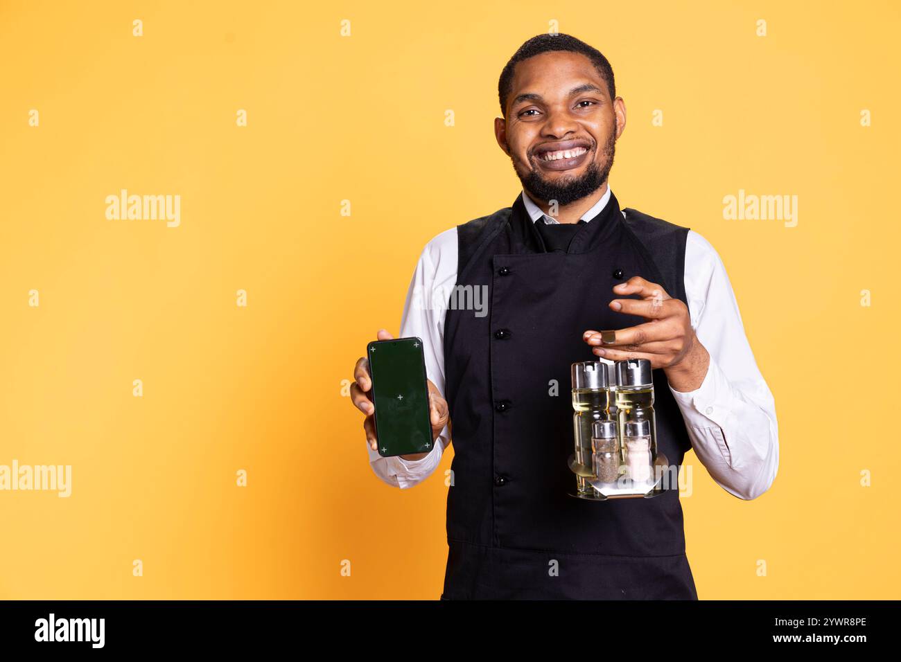 Smiling waiter in uniform presenting a device with isolated chroma key ...