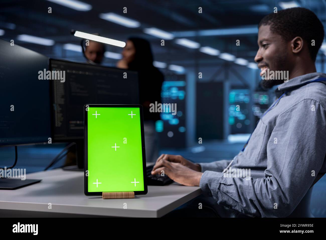 Smiling man working on green screen tablet in modern data center. Happy IT specialist doing IT ...