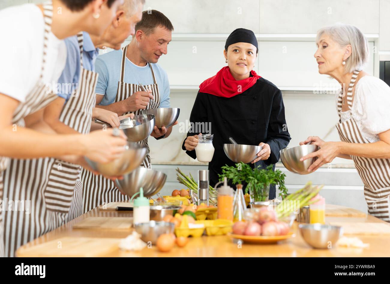 Positive middle-aged woman chef of cooking course teaching attendees ...
