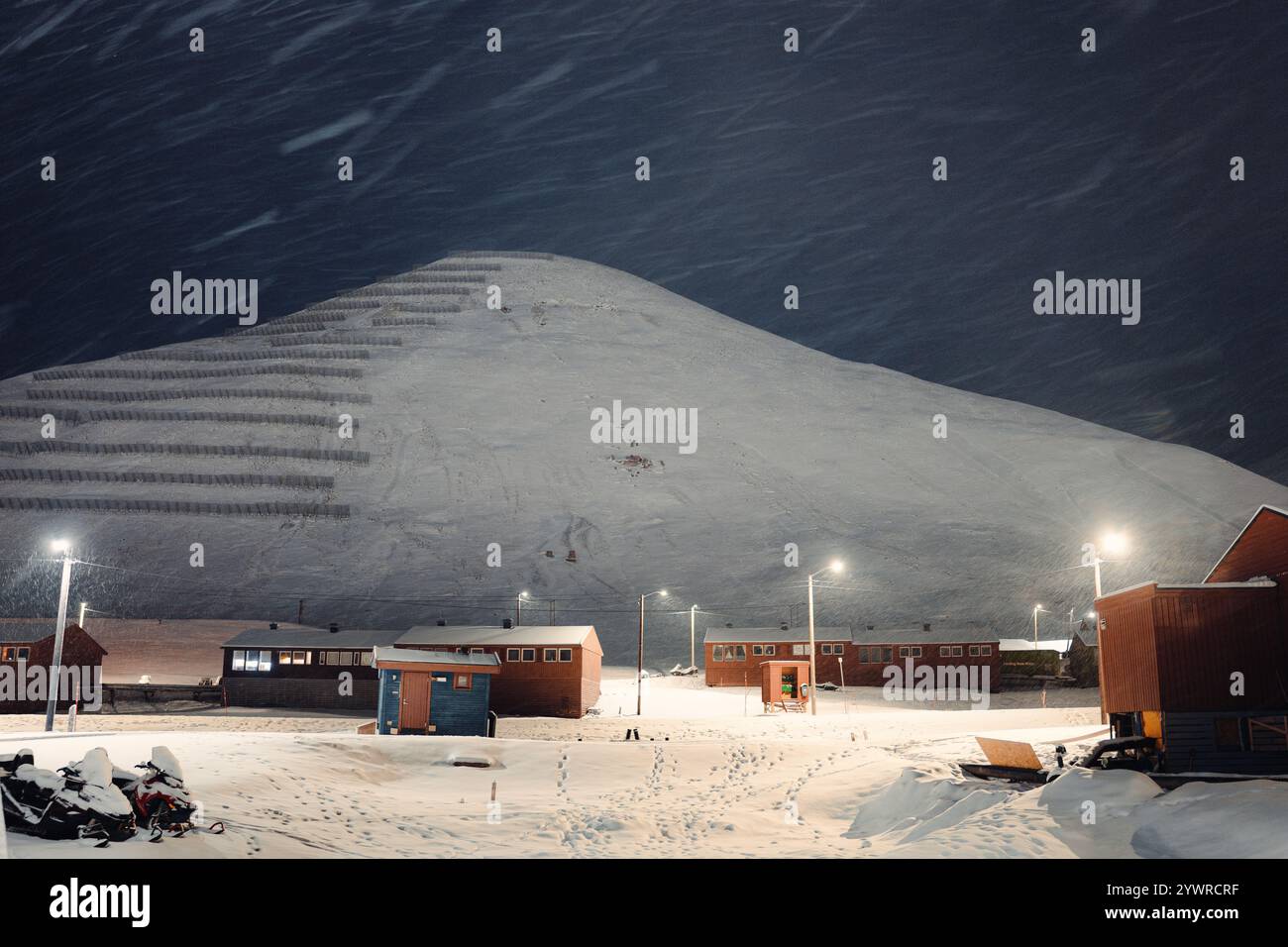 Brown cabins under snowy mountain with avalanche barriers Longyearbyen ...