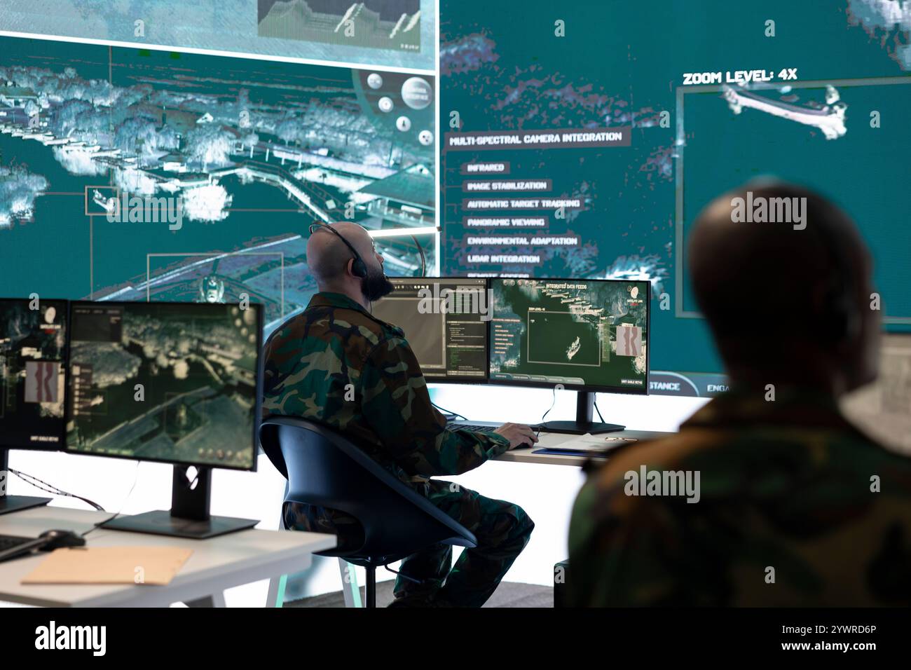 Military staff reviewing CCTV satellite imagery on a big screen in monitoring room, working on a ...