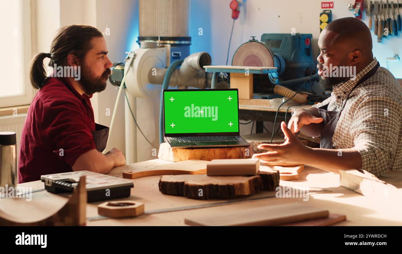 Woodworker looking over blueprints on green screen laptop in CAD software with apprentice ...