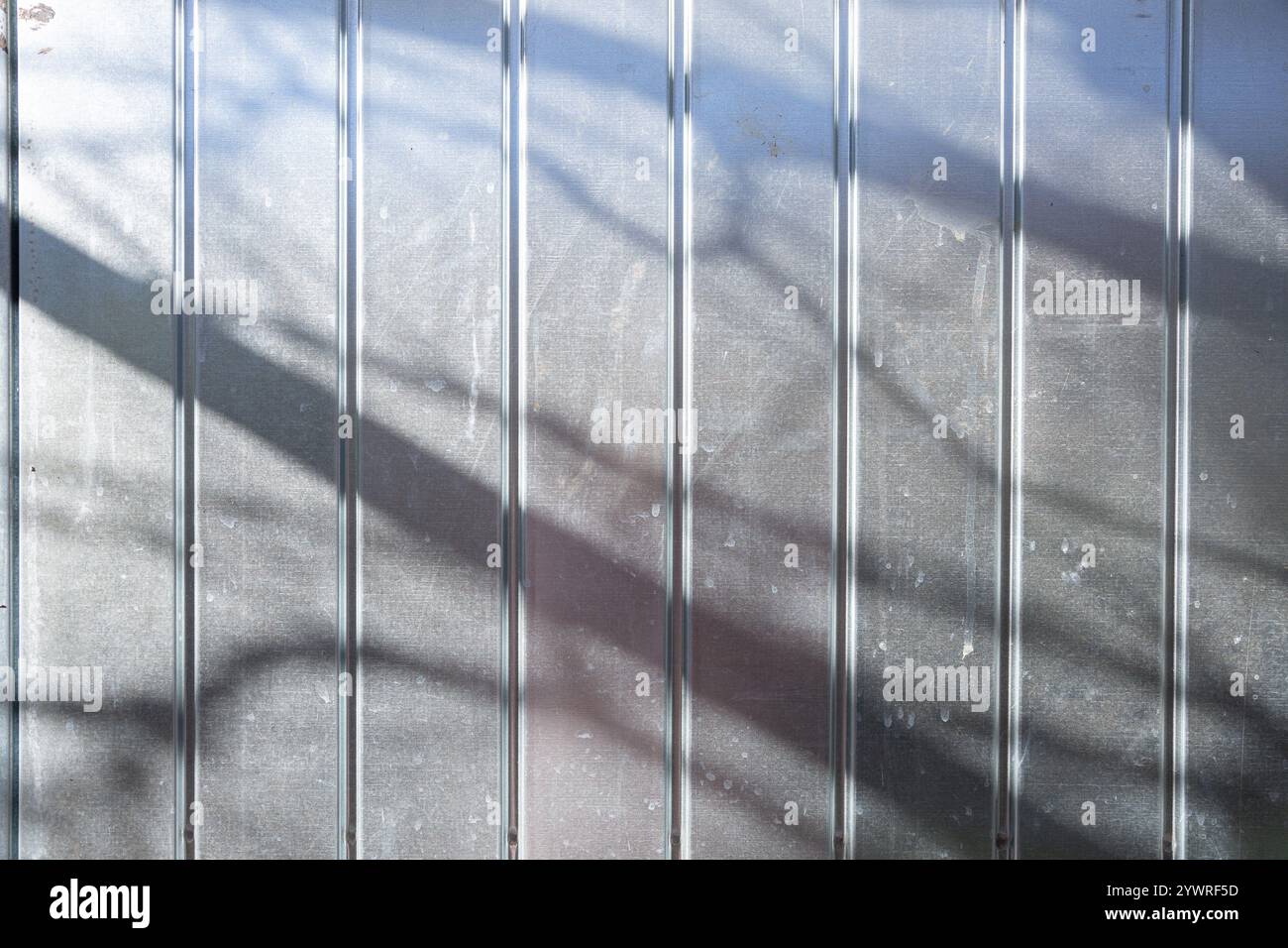 A detailed close up of a metallic fence casting a shadow on the ground ...