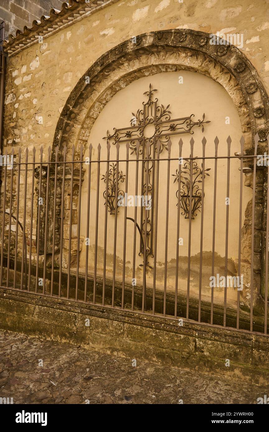 A detailed wrought iron cross adorns an ancient stone wall, encased ...