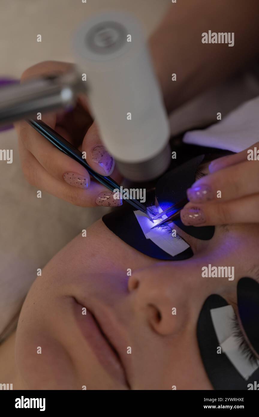 A woman undergoing eyelash extension procedure using an ultraviolet ...