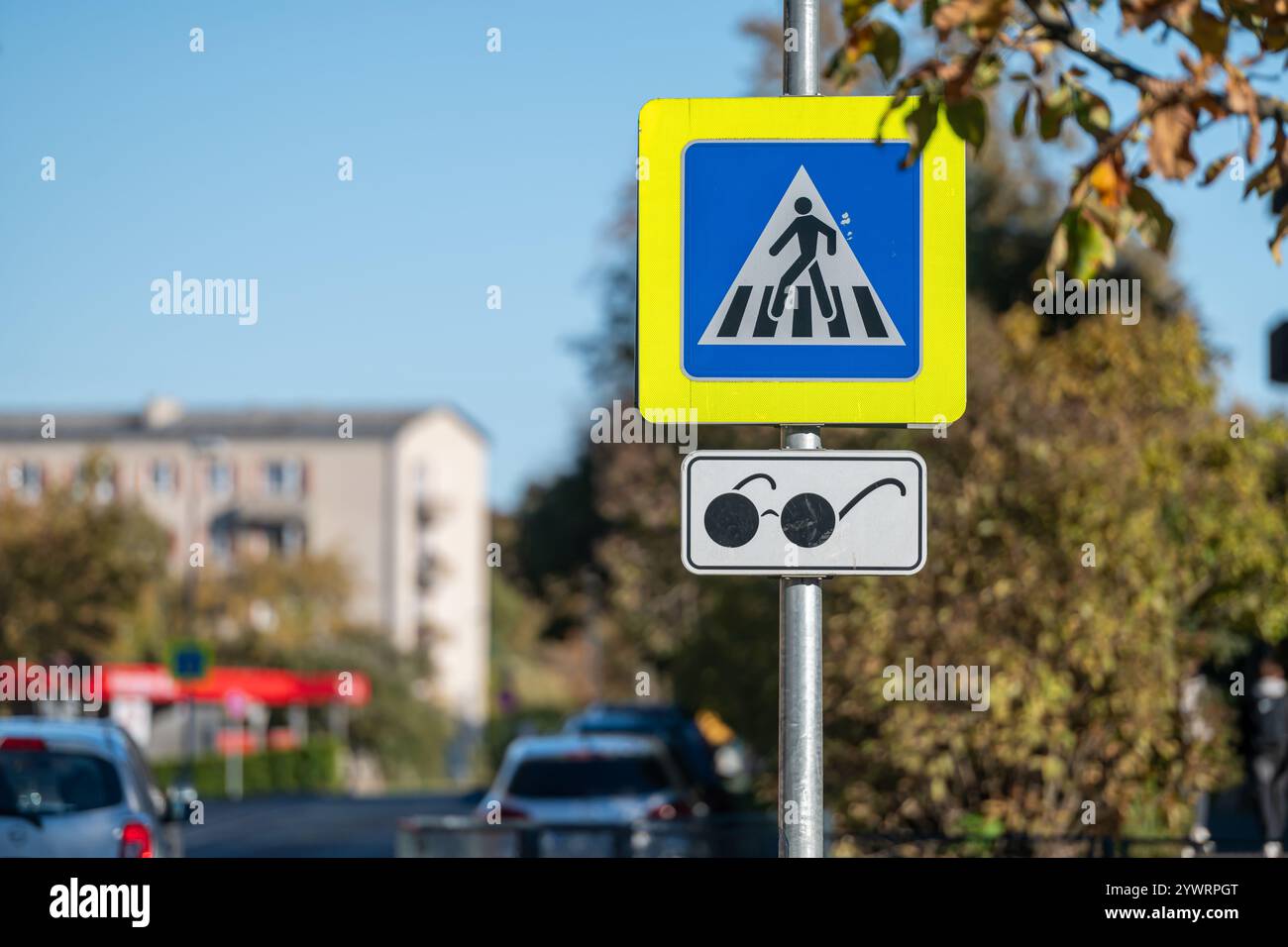 A bright yellow pedestrian crossing sign stands near colorful autumn ...