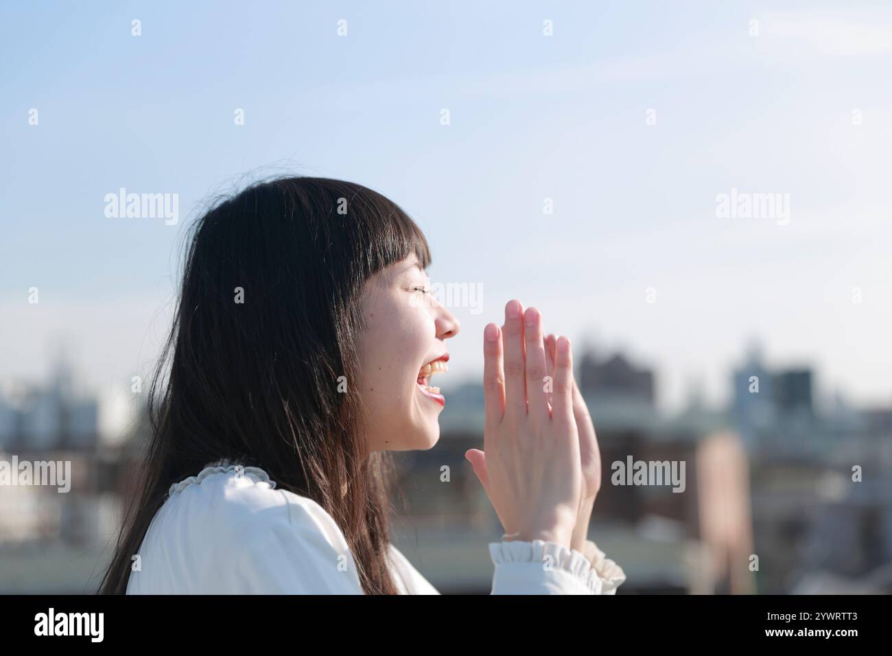 Woman on rooftop holding hands in front of mouth and shouting Stock ...