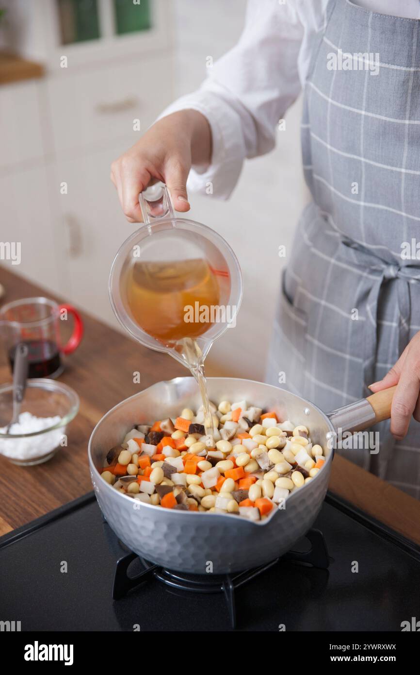 Woman pouring broth into a pot with soya beans and vegetables Stock ...