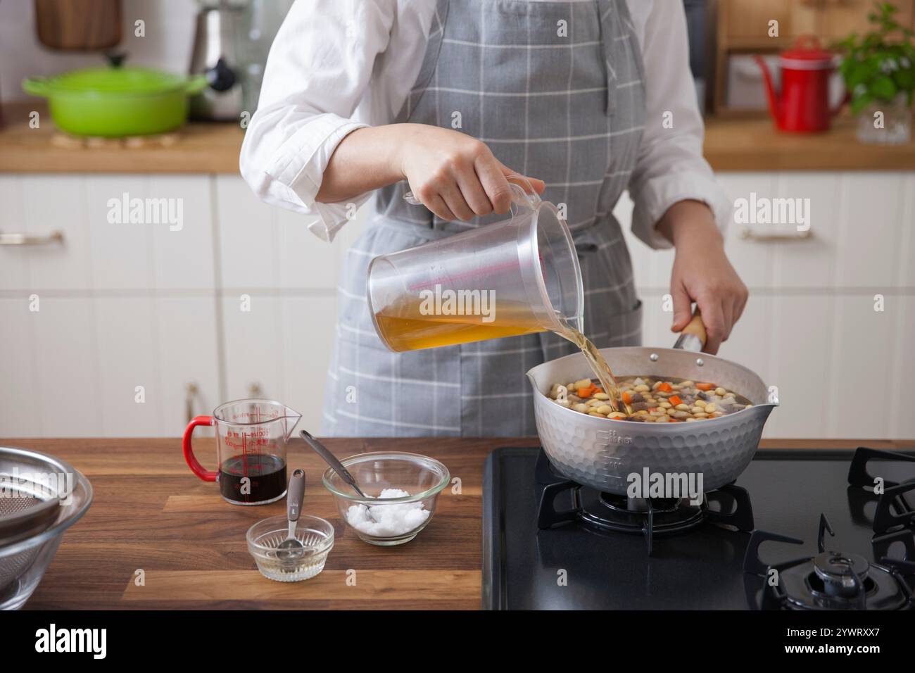 Woman pouring broth into a pot with soya beans and vegetables Stock ...