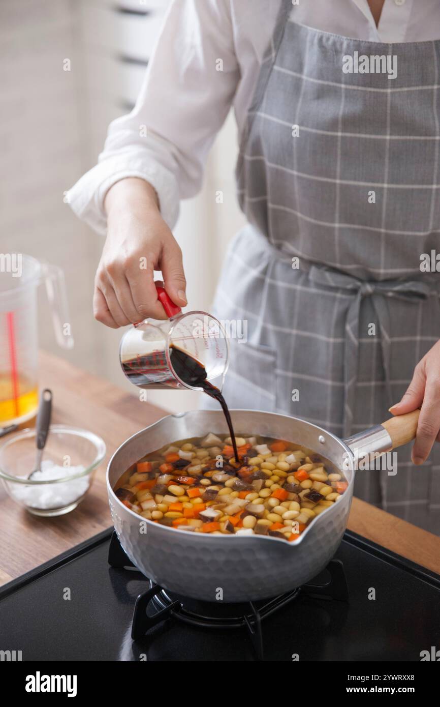 Woman pouring soy sauce into a pot with soya beans and vegetables Stock ...