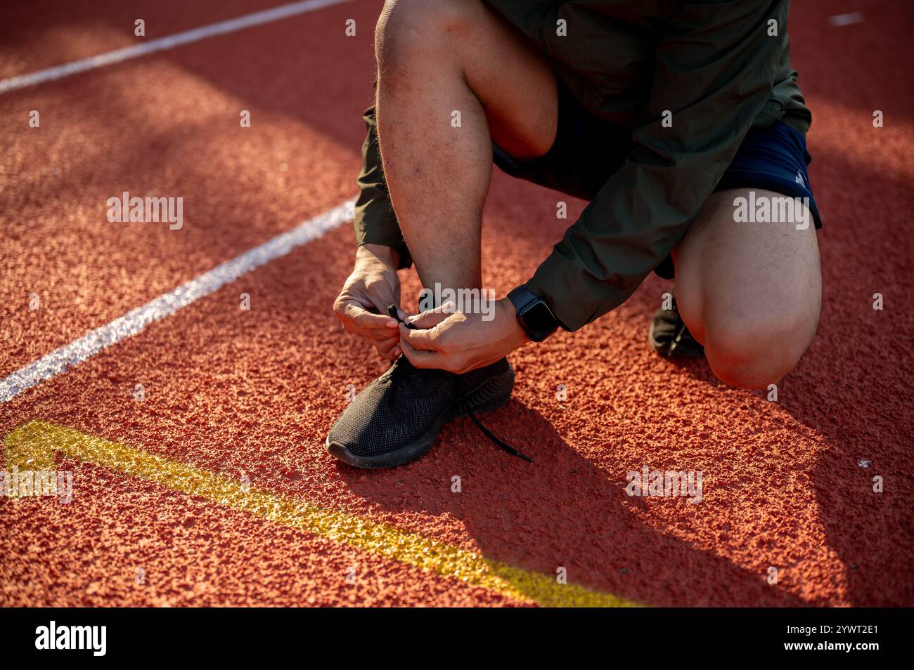 A close-up of a strong, athletic male runner tying his running shoes ...