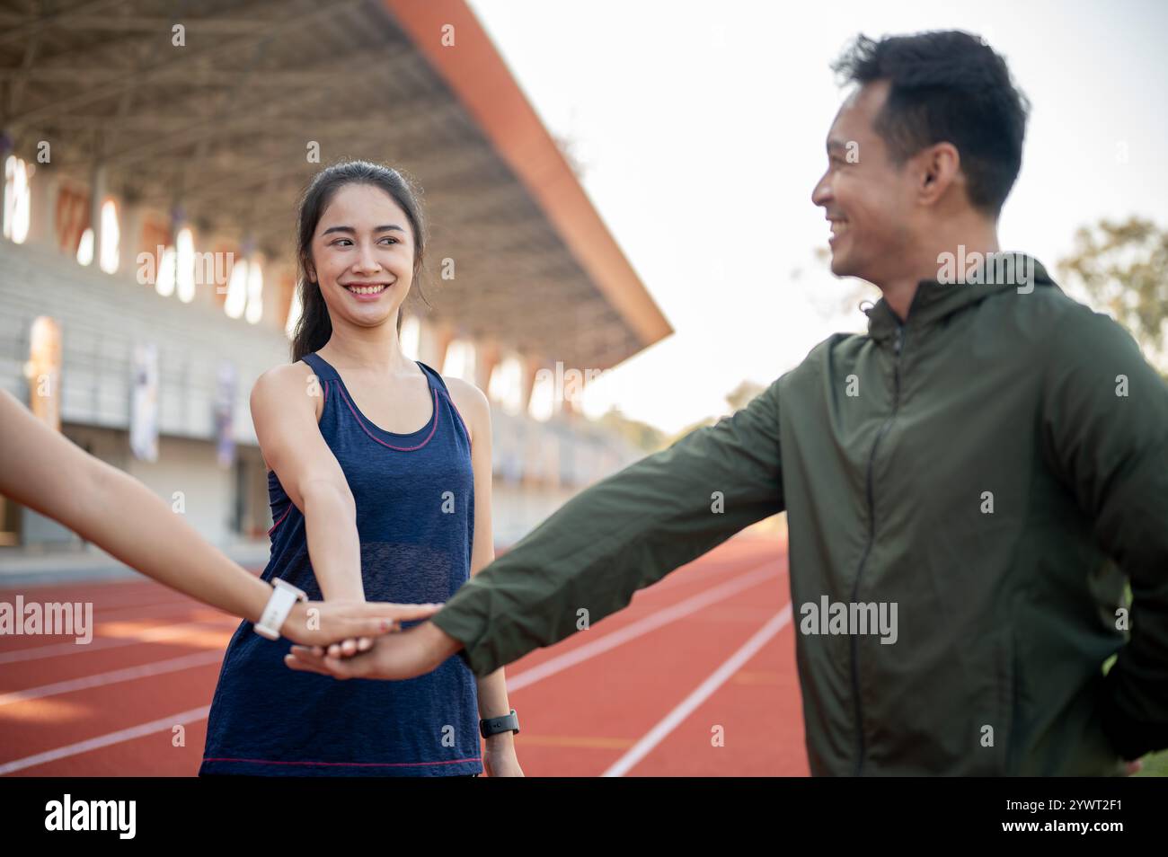 A group of cheerful Asian runners puts their hands together in a ...