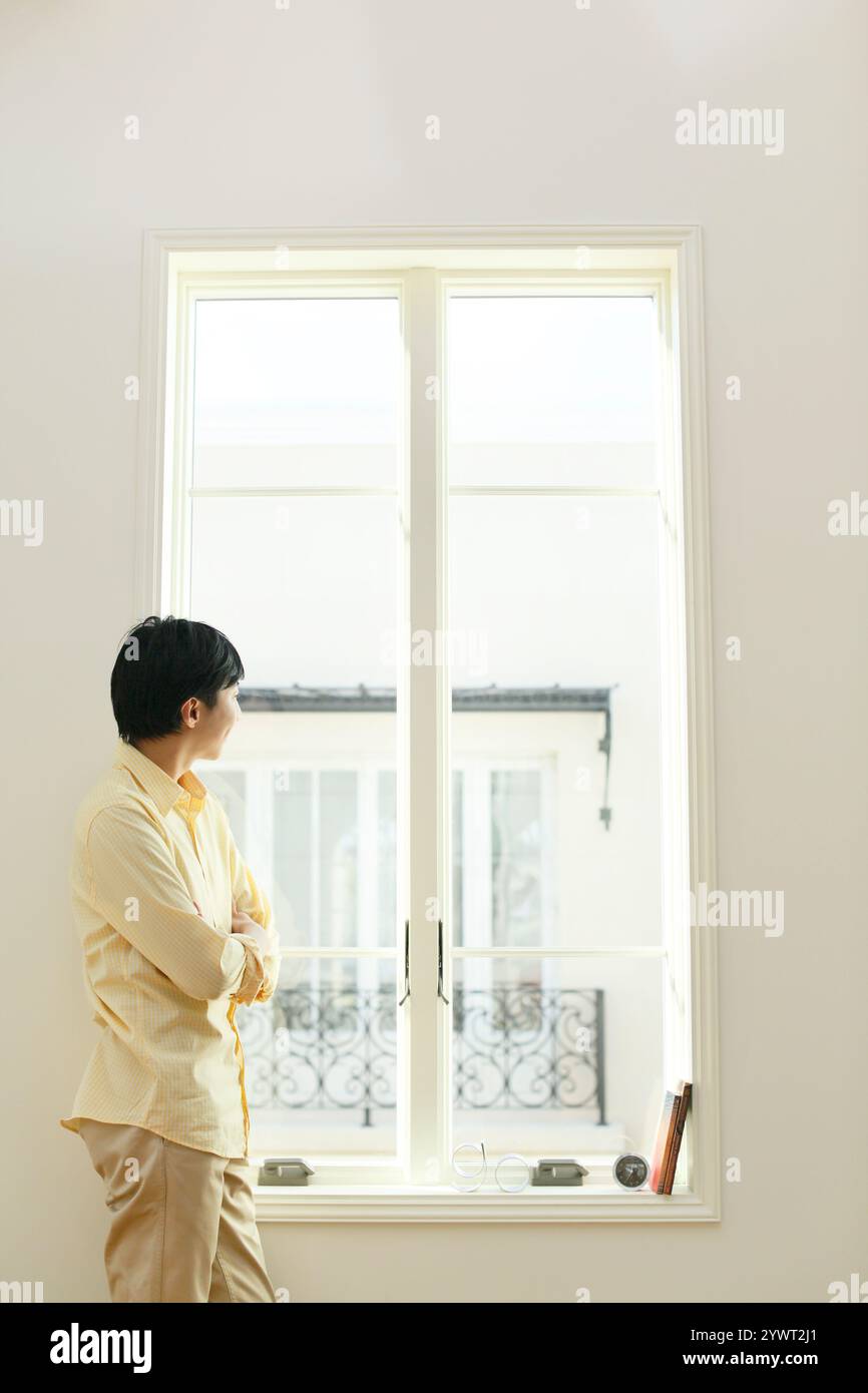 Man looking out of large window in living room Stock Photo - Alamy