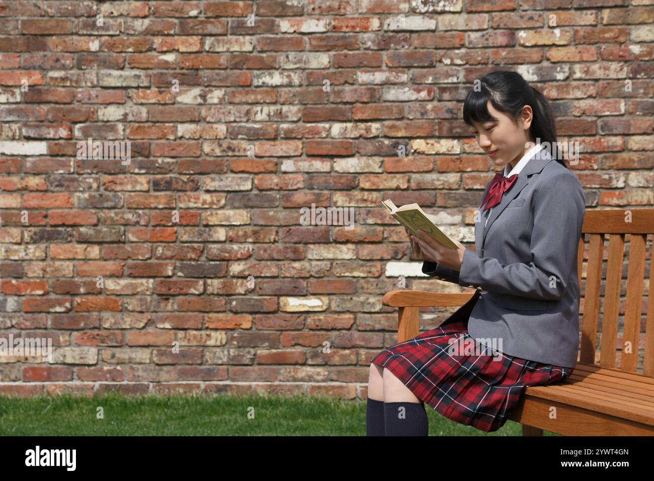 Girl in uniform reading a book on a bench Stock Photo - Alamy