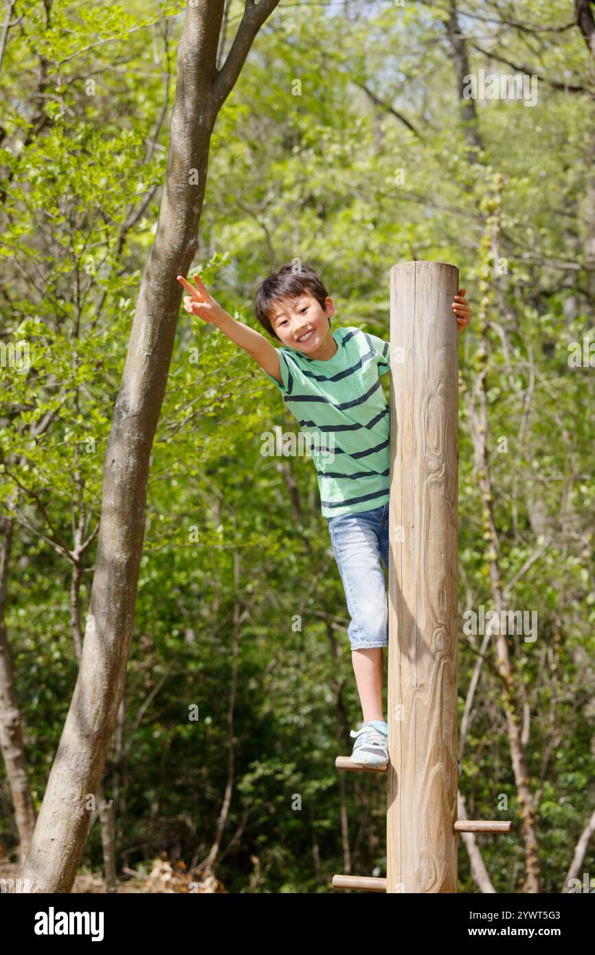 Boy climbing on log in park Stock Photo - Alamy