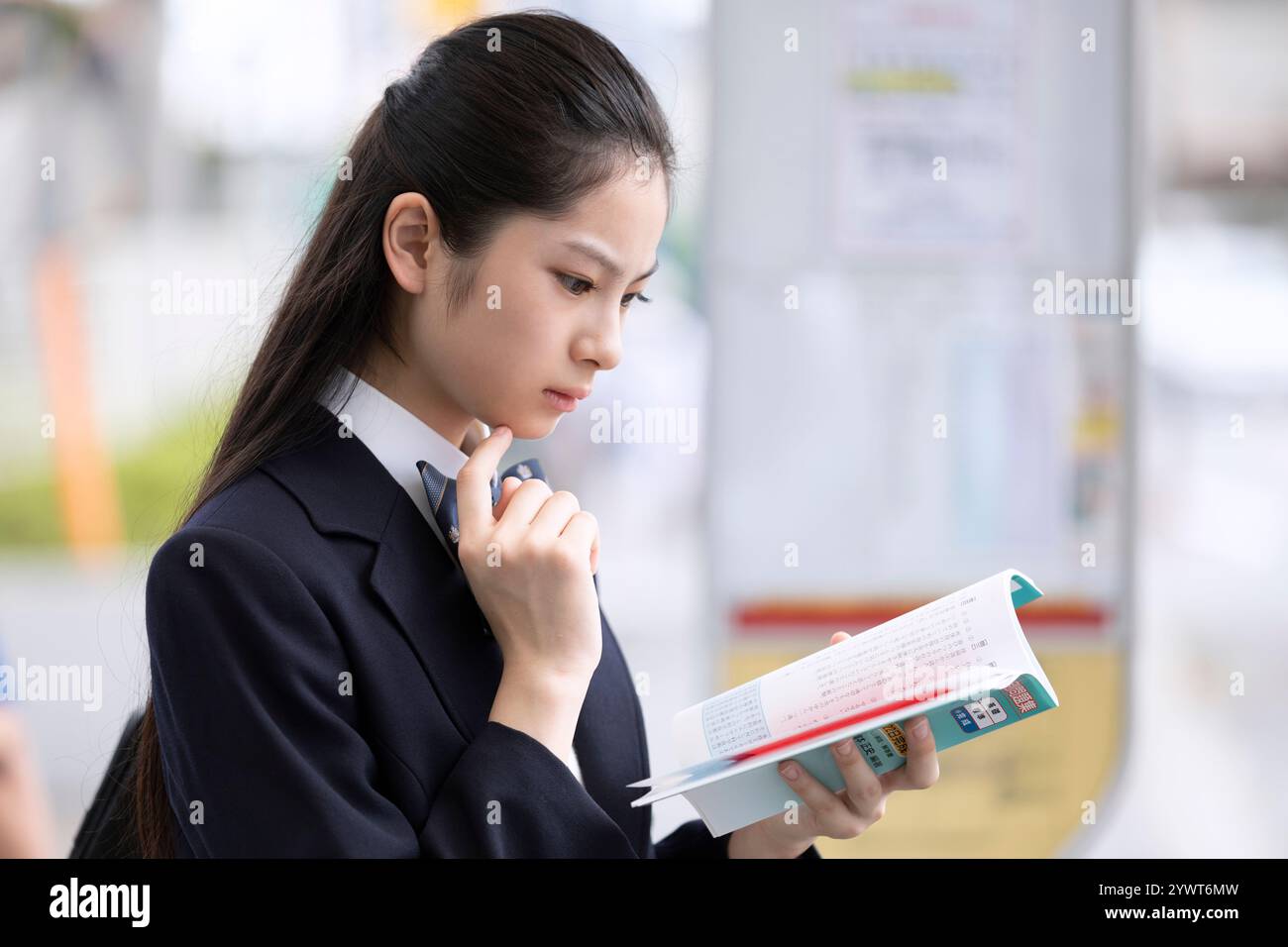 Female high school student waiting for bus while studying Stock Photo ...