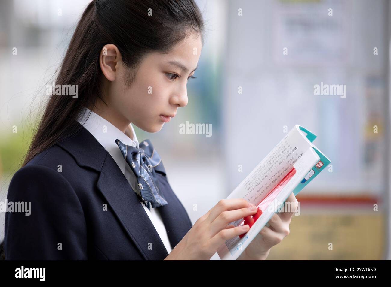 Female high school student waiting for bus while studying Stock Photo ...