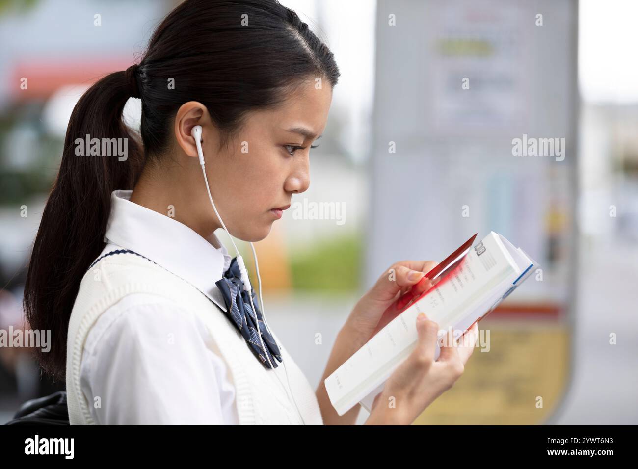 Female high school student waiting for bus while studying Stock Photo ...