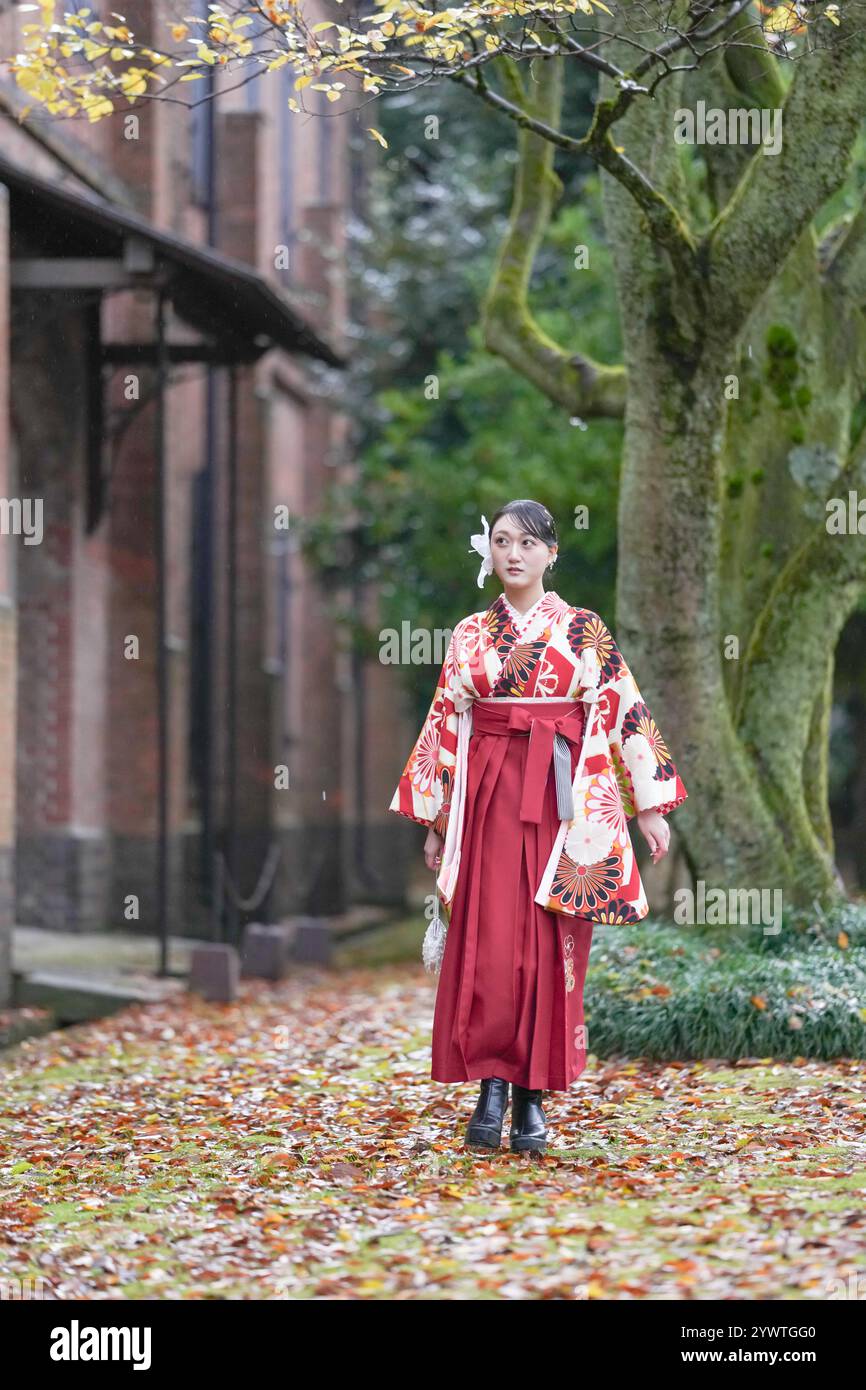 A Japanese woman in her 20s walks in front of a large tree and ...
