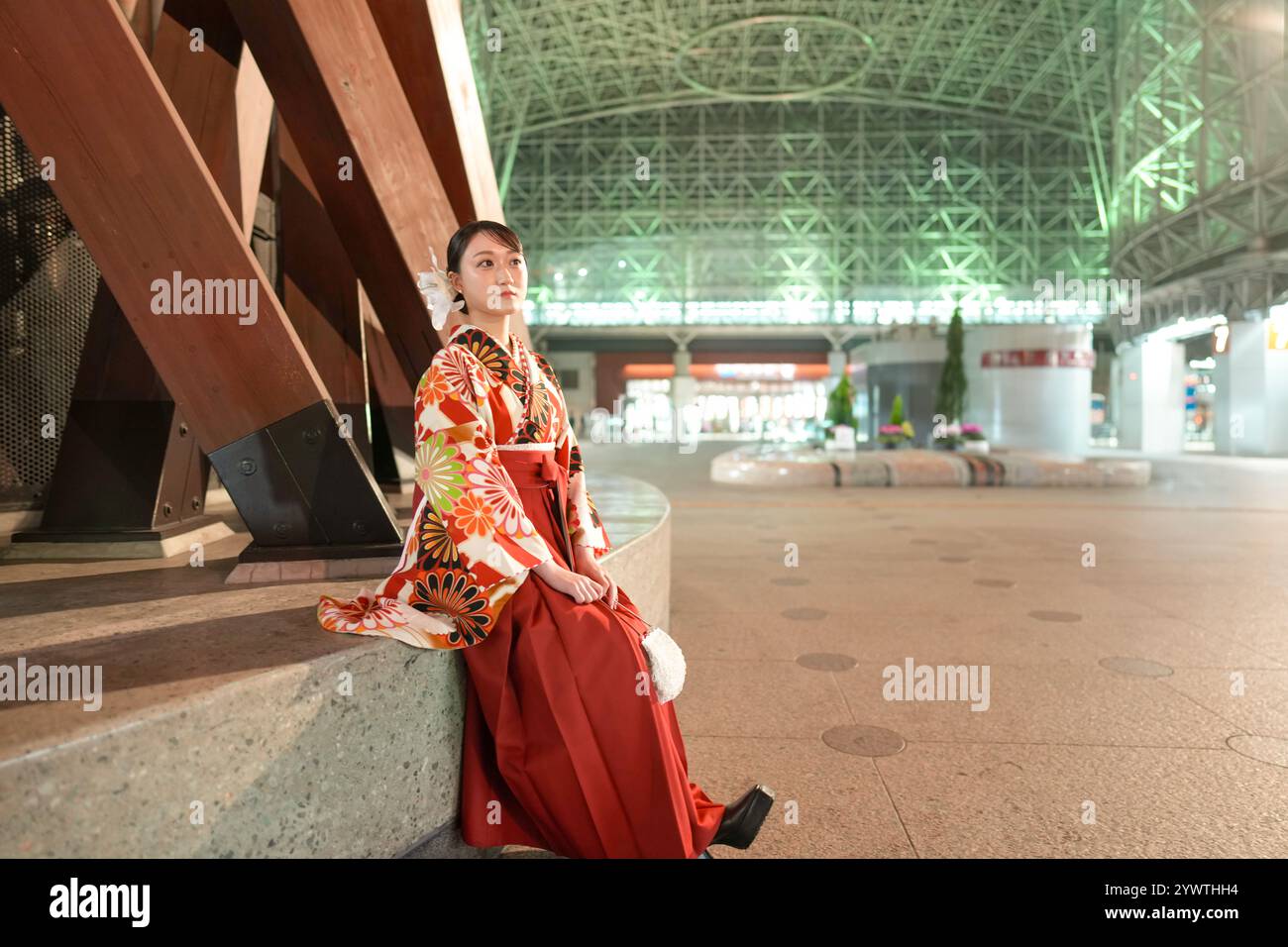 A Japanese woman in her 20s sits at an illuminated train station in ...