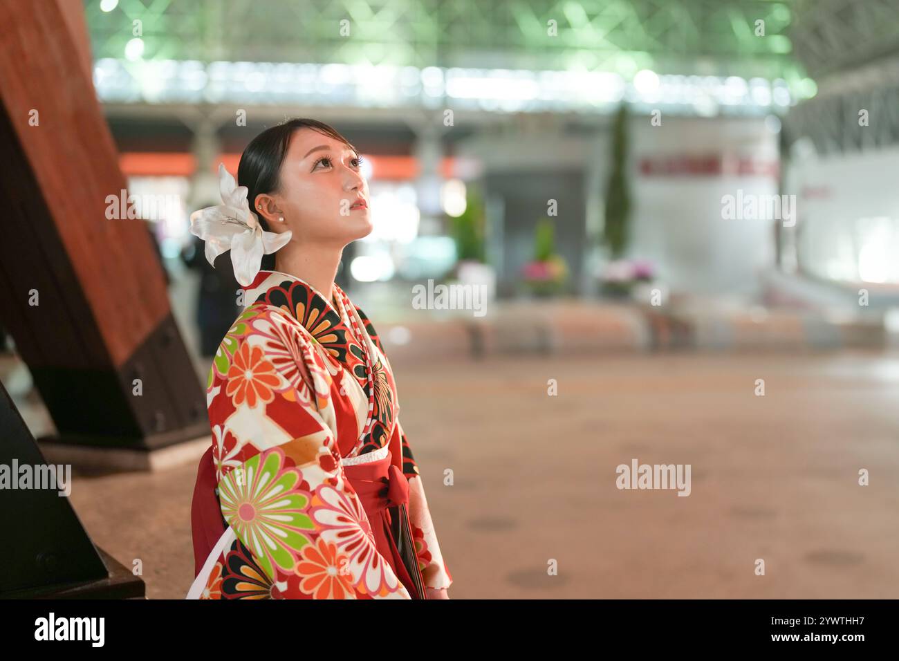A Japanese woman in her 20s sits at an illuminated train station in ...