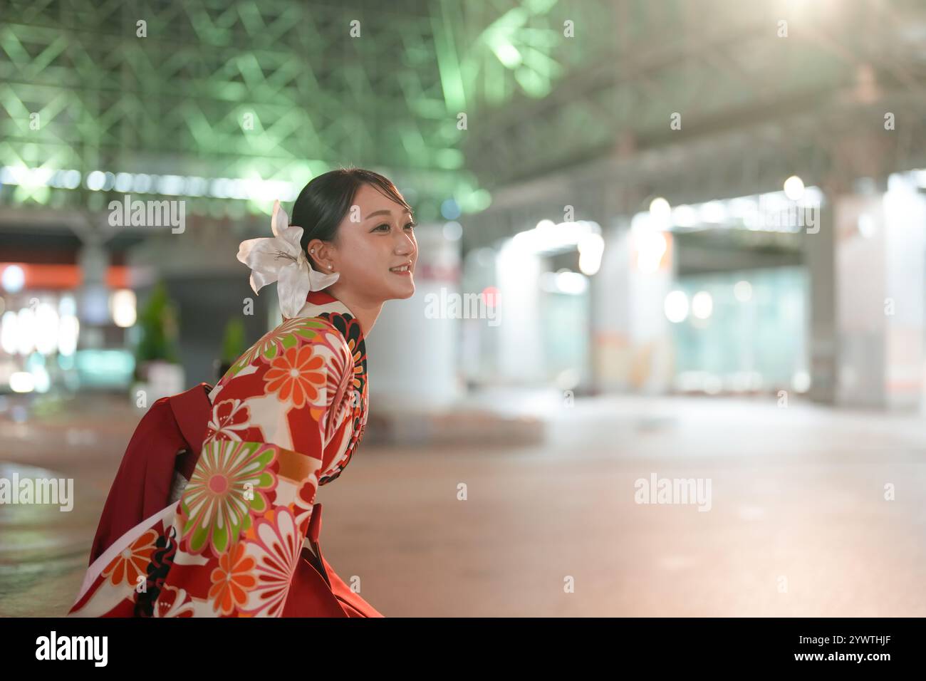 A Japanese woman in her 20s sits at an illuminated train station in ...