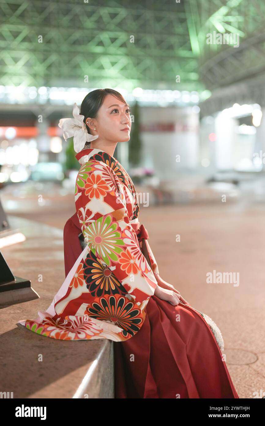 A Japanese woman in her 20s sits at an illuminated train station in ...