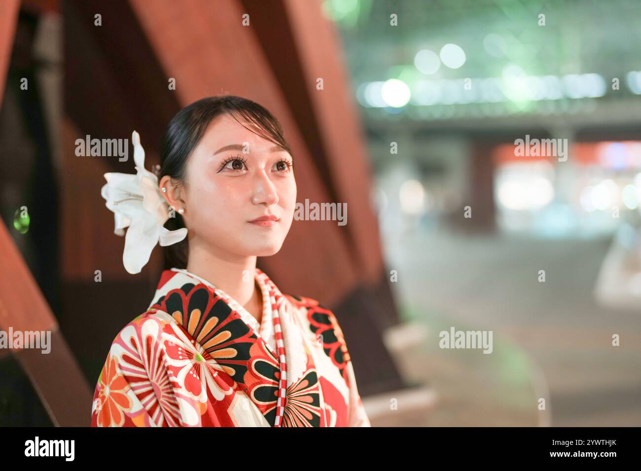 A Japanese woman in her 20s sits at an illuminated train station in ...