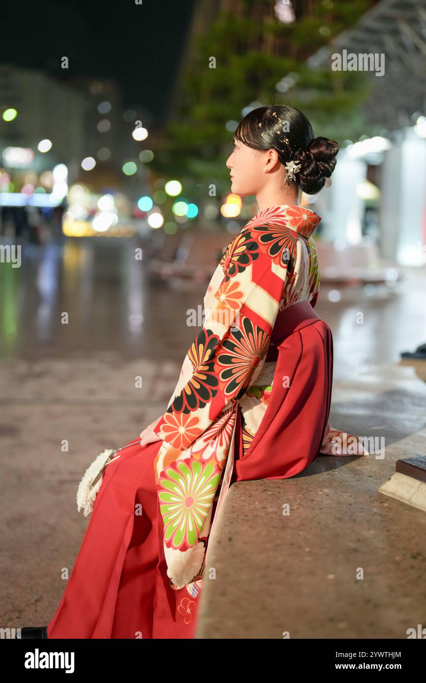 A Japanese woman in her 20s sits at an illuminated train station in ...
