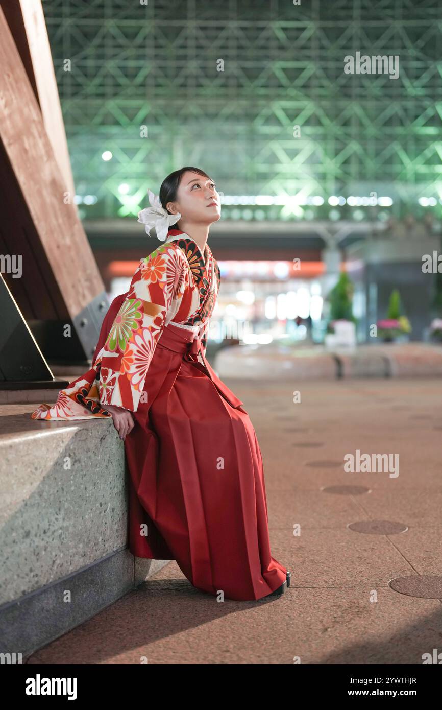 A Japanese woman in her 20s sits at an illuminated train station in ...