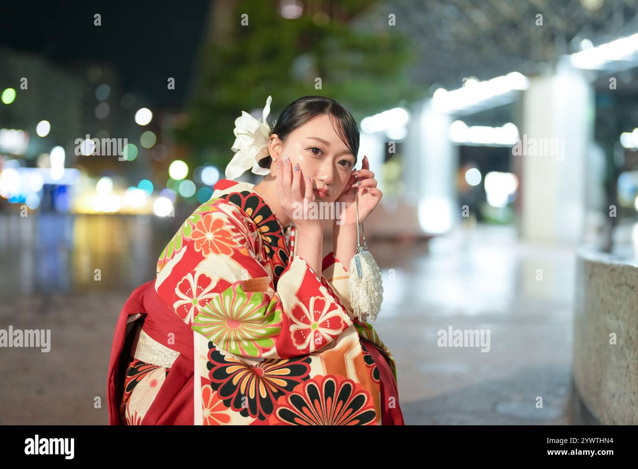 A Japanese woman in her 20s sits at an illuminated train station in ...