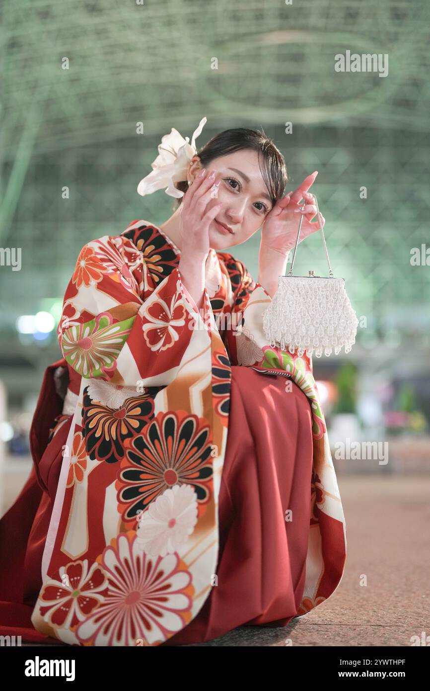 A Japanese woman in her 20s sits at an illuminated train station in ...