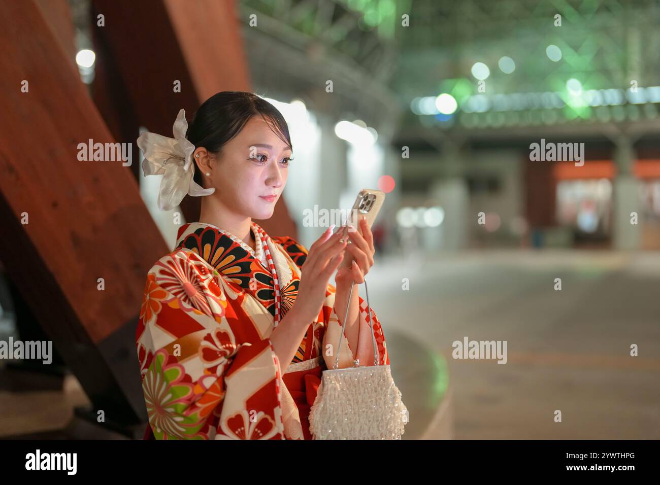 A Japanese woman in her 20s sits at an illuminated train station in ...