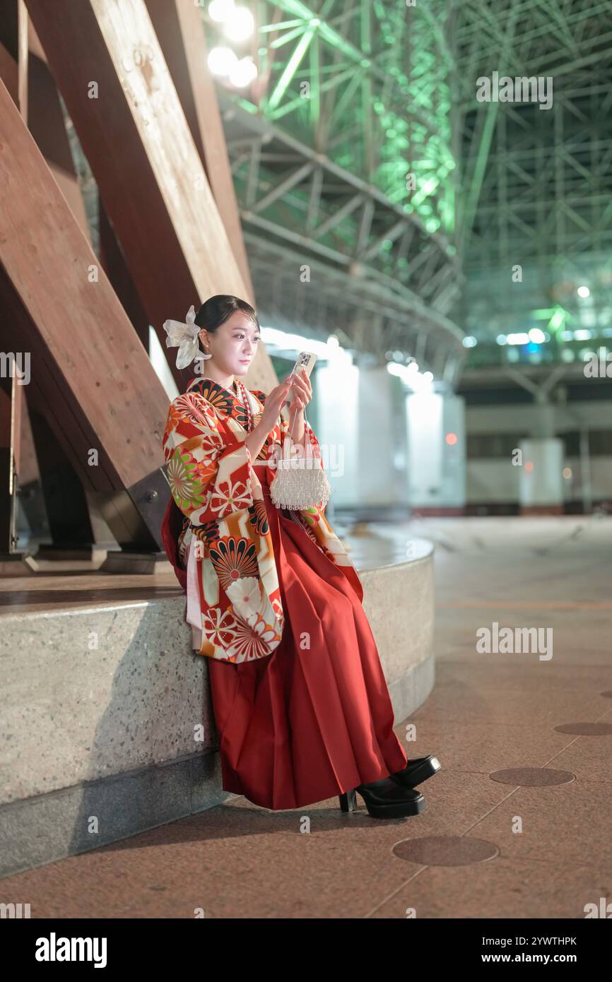 A Japanese woman in her 20s sits at an illuminated train station in ...