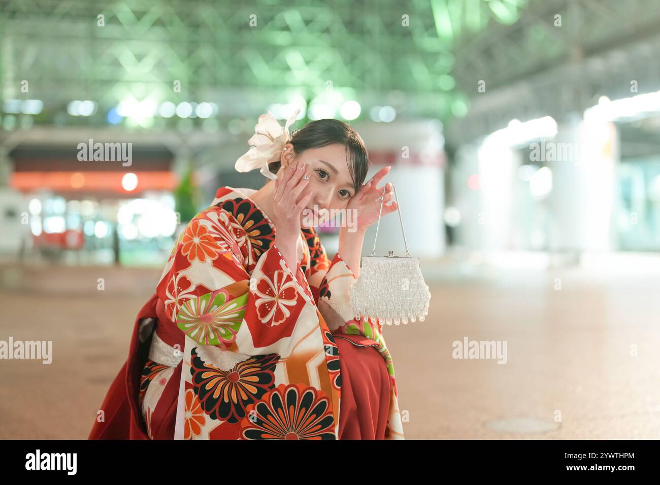 A Japanese woman in her 20s sits at an illuminated train station in ...