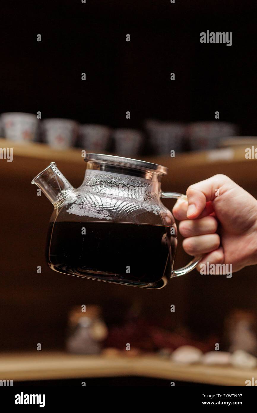 A hand is holding a beautifully designed glass coffee pot filled with ...